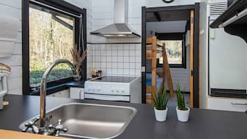 Cozinha compacta com pia, fogão e janela com vista para área arborizada.