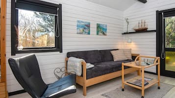 Uma sala de estar aconchegante com um sofá cinza escuro, uma poltrona de couro preto, uma mesa de centro de madeira e um pequeno aparador com objetos decorativos.