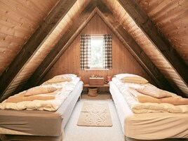 Quarto de sótão aconchegante com duas camas, uma mesinha e uma janela com cortinas.
