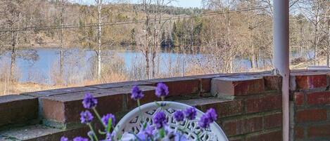 Um pátio com vista para um lago e árvores, uma parede de tijolos e um prato decorativo branco com flores roxas.
