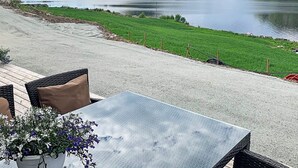 Um pátio com mesa e cadeiras com vista para um lago e colinas.
