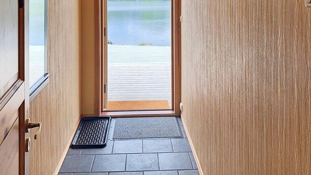 Uma porta de madeira dá para um deck com vista para um lago e montanhas.