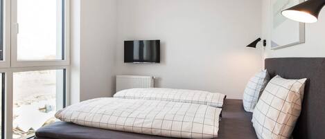 Quarto moderno com uma cama grande, uma TV de tela plana e uma janela.