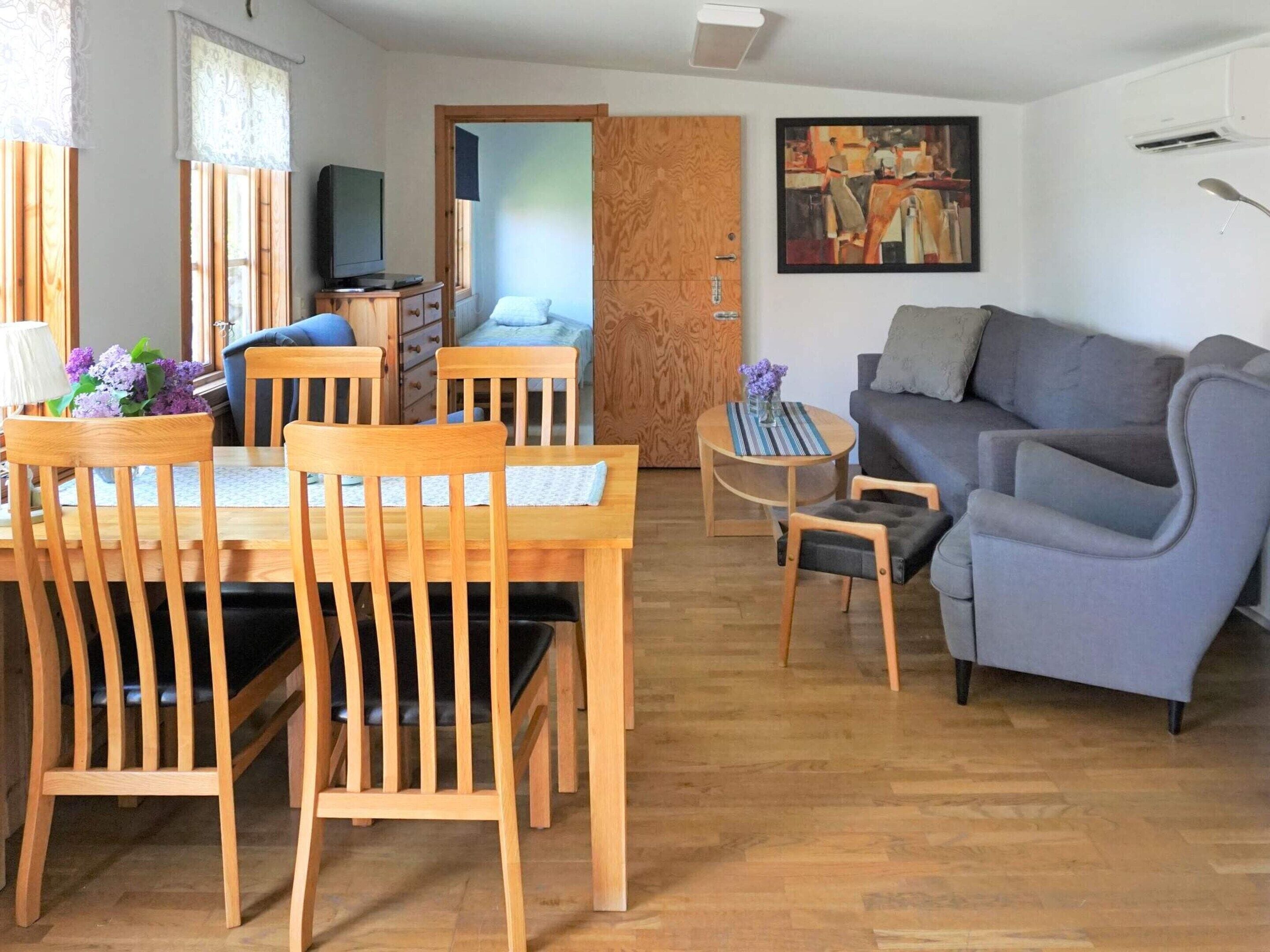 Sala de estar com sofá, mesa de jantar com cadeiras, televisão e um quadro na parede.