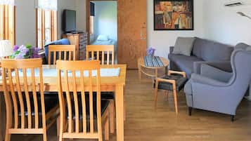 Sala de estar com sofá, mesa de jantar com cadeiras, televisão e um quadro na parede.