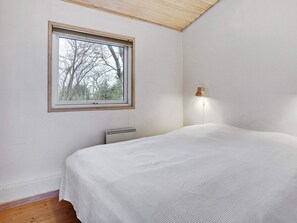 Quarto com uma cama de solteiro, radiador, janela com vista para árvores e luminária fixada na parede.
