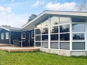 Uma casa moderna com uma ampla extensão de vidro, um deck com mobiliário de exterior e um gramado bem cuidado.