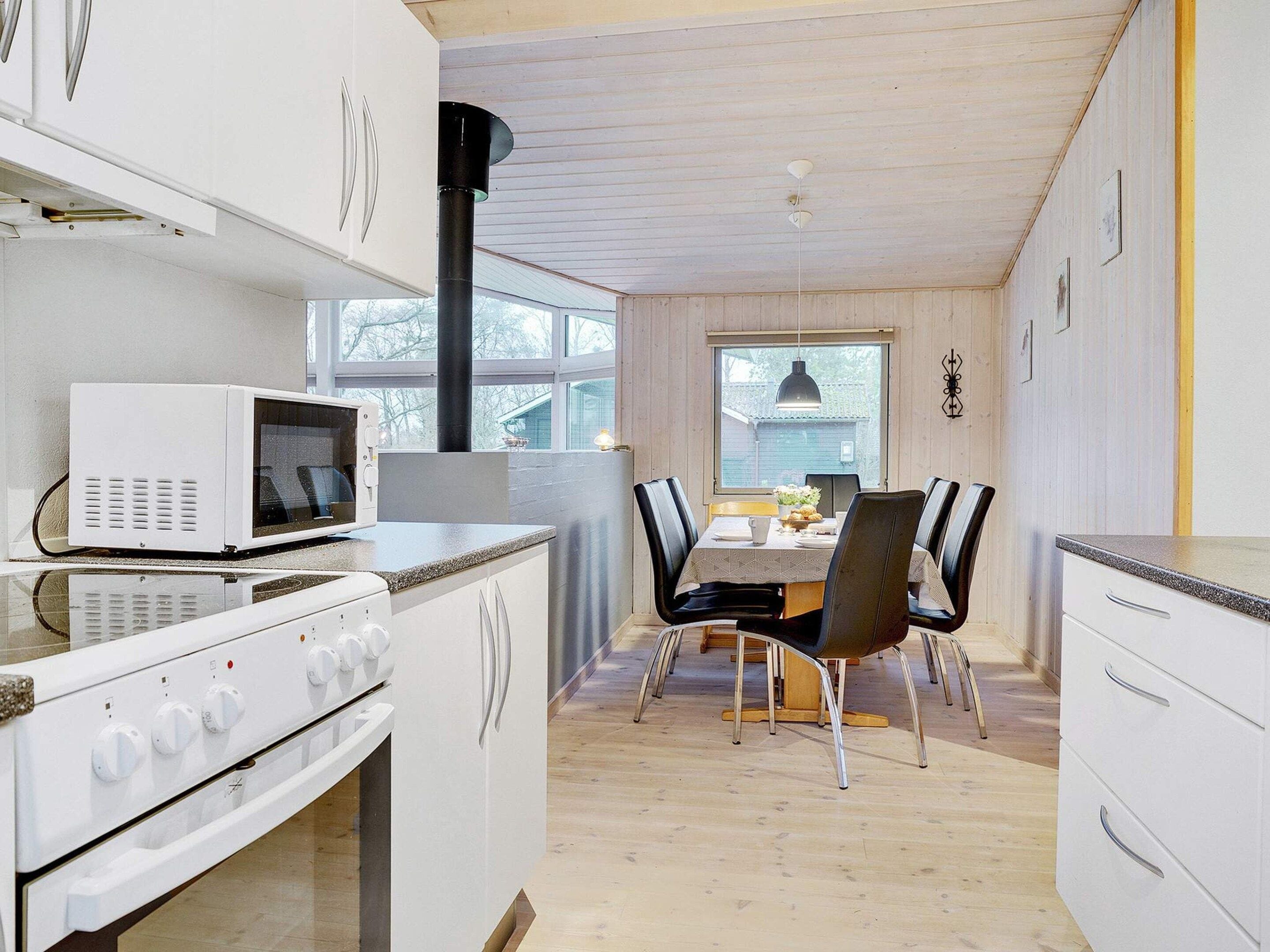 Cozinha moderna com armários brancos, micro-ondas e fogão. Há uma mesa de jantar com cadeiras e uma janela com vista para o exterior.
