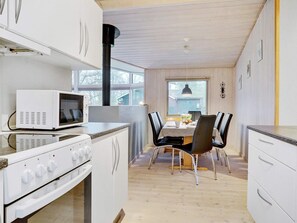 Cozinha moderna com armários brancos, micro-ondas e fogão. Há uma mesa de jantar com cadeiras e uma janela com vista para o exterior.