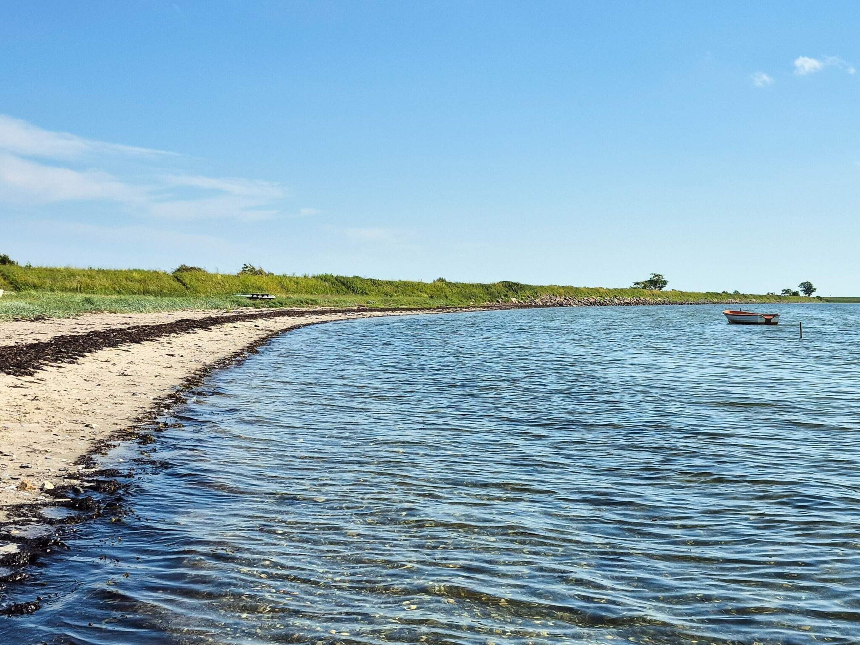 Uma praia com águas cristalinas, um barco e uma linha de costa ao longe.