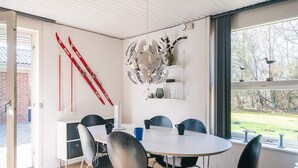 Uma sala de jantar moderna com uma mesa redonda, cadeiras pretas e uma grande janela com vista para árvores.
