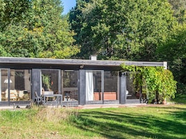 Uma casa moderna com grandes janelas de vidro, um pátio com mobiliário externo e um jardim.