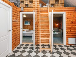 Quarto em estilo de cabana de tronco com piso xadrez, uma cama, uma escrivaninha e uma escada que leva a um mezanino com caixas de madeira.
