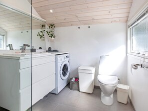 Uma casa de banho moderna com máquina de lavar roupa, sanita e um espelho grande.