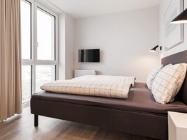 Quarto moderno com uma grande janela, televisão de tela plana e cama com colcha estampada.