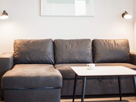 Uma sala de estar moderna com um sofá de couro cinzento, uma mesinha com uma chávena e duas luminárias de parede.