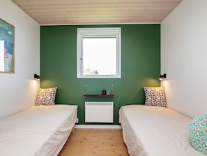 Quarto com duas camas de solteiro, uma janela, um radiador e uma pequena prateleira com objetos.