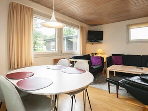 Uma sala de estar moderna com uma mesa de jantar redonda, sofás, uma TV e janelas grandes.