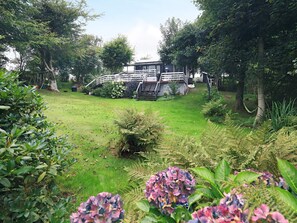 Um jardim com uma ponte de madeira que leva a uma casa com fachada branca e escadaria.