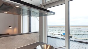 Uma cozinha moderna com uma janela ampla, uma panela de aço inoxidável em um fogão por indução, e a marca Siemens visível no teto.