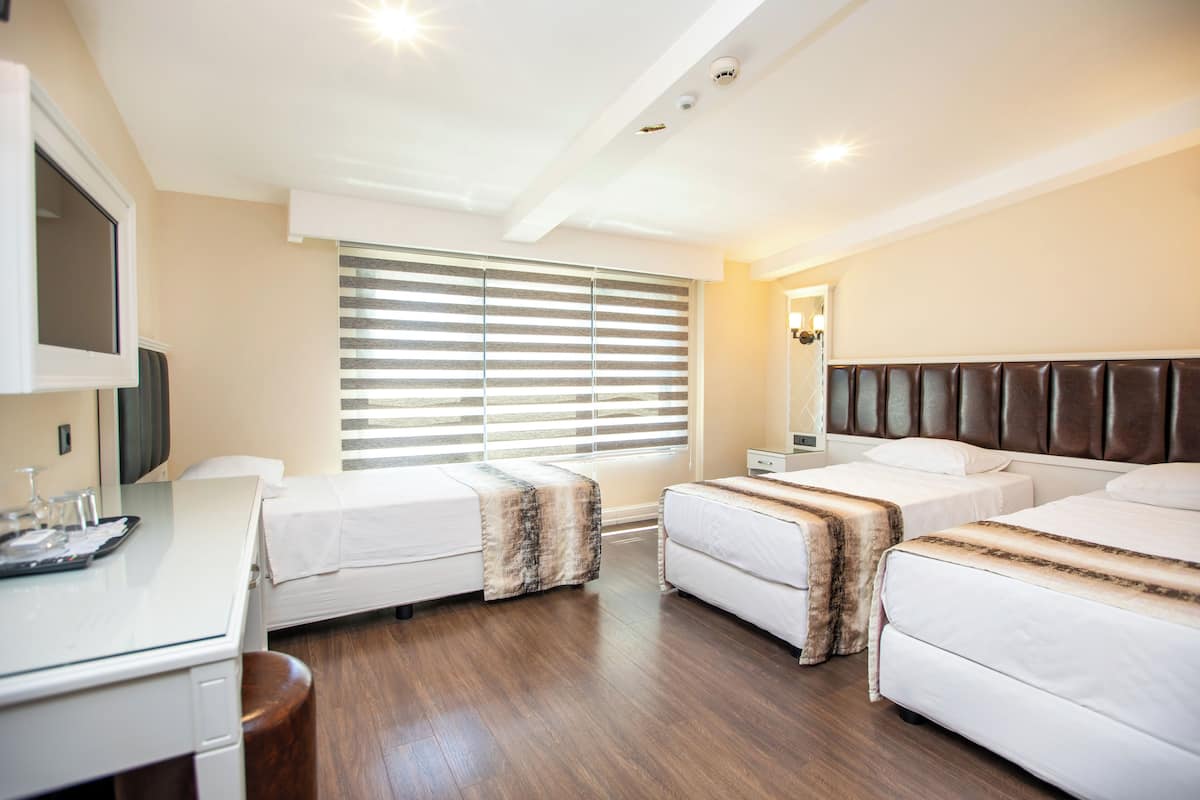 Quarto de hotel com duas camas, uma escrivaninha, uma televisão e uma janela com persianas.