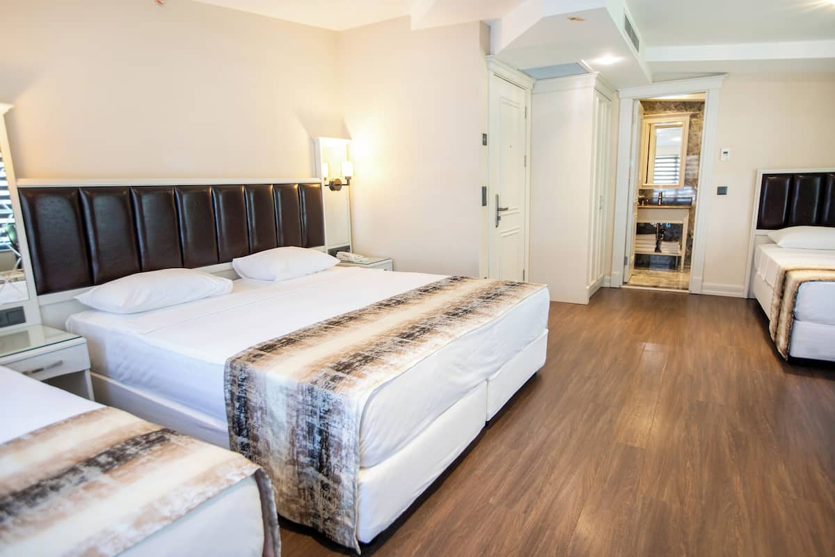 Quarto de hotel com uma cama grande, mesas de cabeceira, um guarda-roupa e um banheiro visível por uma porta aberta.