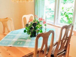 Uma mesa de jantar com toalha xadrez, rodeada por cadeiras de madeira. Um vaso com flores vermelhas está colocado sobre a mesa.