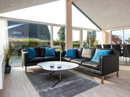 Uma área de estar moderna com sofá seccional, mesa de centro redonda e janelas amplas com vista para o exterior.