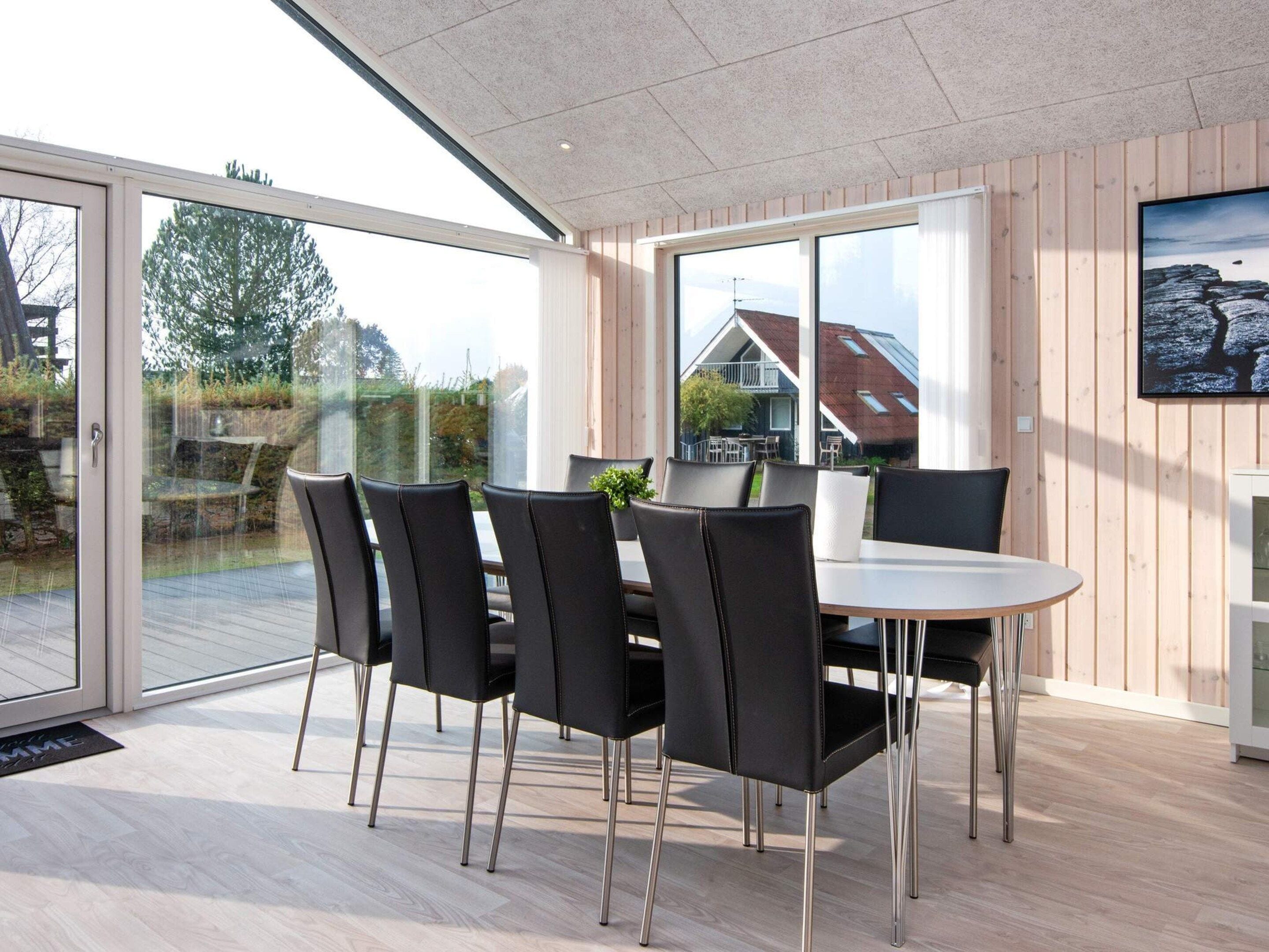 Uma zona de refeições moderna com porta de vidro que dá para um terraço, uma mesa redonda e cadeiras pretas com pernas de metal.