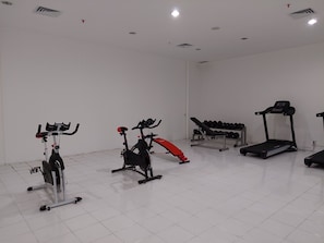Uma academia com equipamentos de cardio, bancos de peso e halteres.