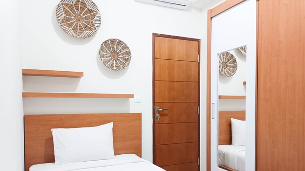 Quarto de hotel bem arrumado com cabeceira de madeira, cama com roupa de cama branca, porta de madeira e dois objetos decorativos fixados na parede.
