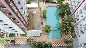 Vista aérea de um edifício residencial com piscina, rodeado por palmeiras e um padrão quadriculado no chão.