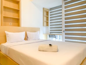 Uma cama bem arrumada com lençóis brancos, cabeceira de madeira e uma janela com persianas.