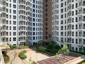 Edifício residencial alto com várias varandas, um pátio central com vegetação e uma combinação de paredes externas brancas e bege.