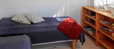 Um quarto pequeno e aconchegante com uma cama de solteiro, uma mesa de cabeceira de madeira e uma estante.