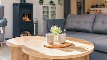Uma sala de estar moderna com lareira, sofá cinza e mesa redonda de madeira com objetos decorativos.