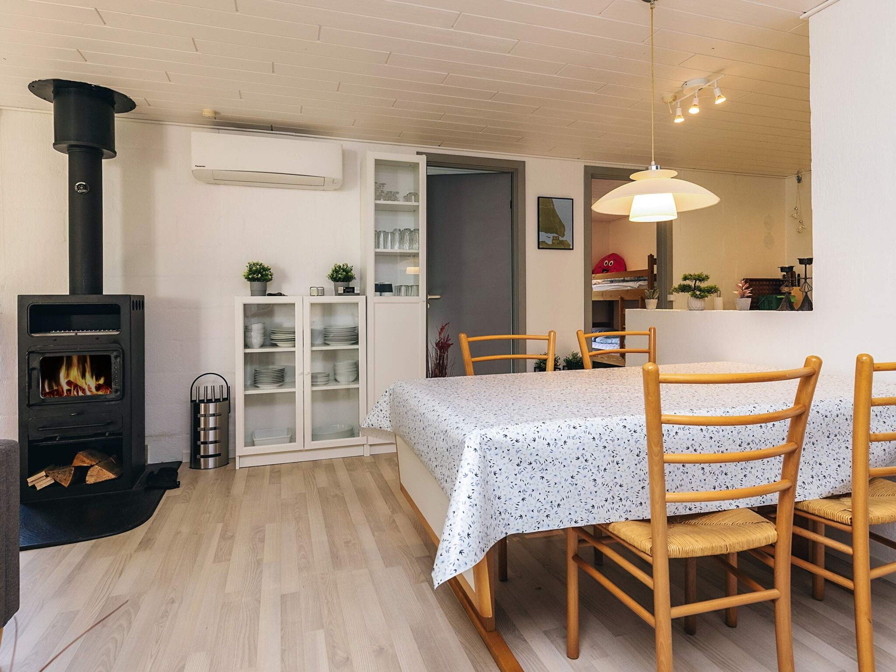 Um quarto acolhedor com lareira a lenha, uma mesa de jantar com cadeiras e um armário com louças.