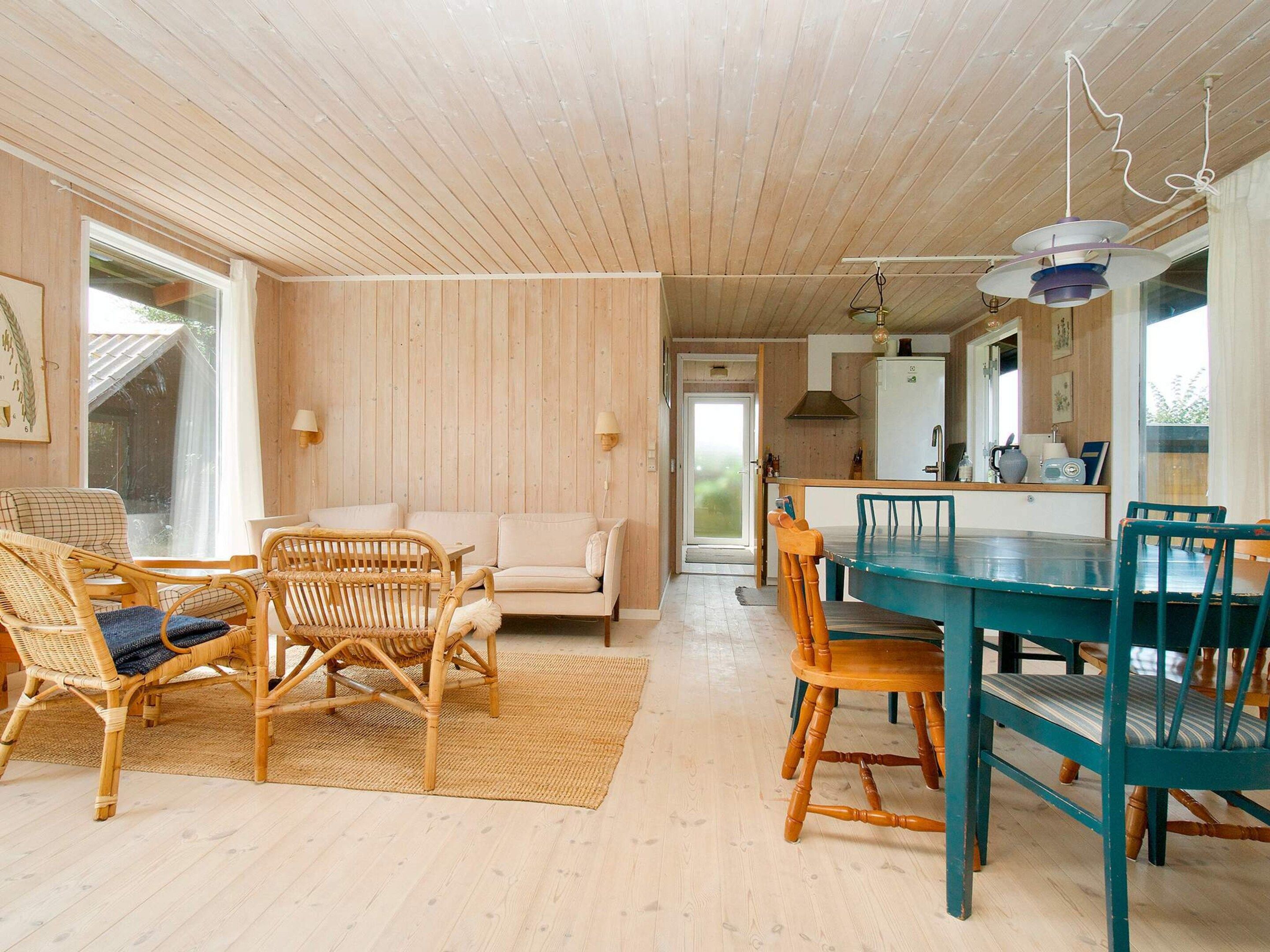 Quarto com piso de madeira, mesa de jantar com cadeiras, sofá e cozinha equipada com geladeira e fogão.