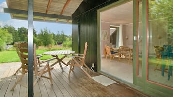 Um deck de madeira com mesa e cadeiras, porta de vidro que dá para um espaço interior com móveis de vime.