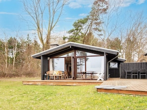 Uma cabana moderna com uma grande porta de vidro, um deck e um espaço de pátio.