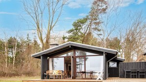 Uma cabana moderna com uma grande porta de vidro, um deck e um espaço de pátio.