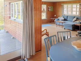 Interior de uma cabana de madeira com um sofá azul, uma mesa de jantar e uma cortina.