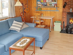 Uma sala de estar aconchegante com um sofá azul, uma mesa de centro de madeira, uma lareira e uma estante repleta de livros e objetos decorativos.