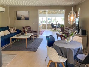 Uma sala de estar moderna com um sofá, cadeiras, uma mesa de centro e uma área de jantar com mesa e cadeiras.