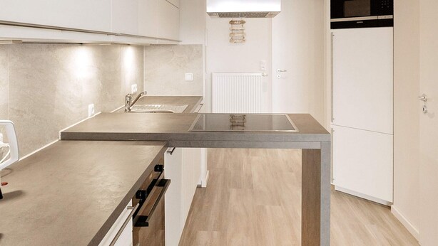 Cozinha moderna com ilha central, eletrodomésticos de aço inoxidável e armários brancos.