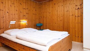 Quarto com painéis de madeira, uma cama, luminária na parede e uma cadeira.