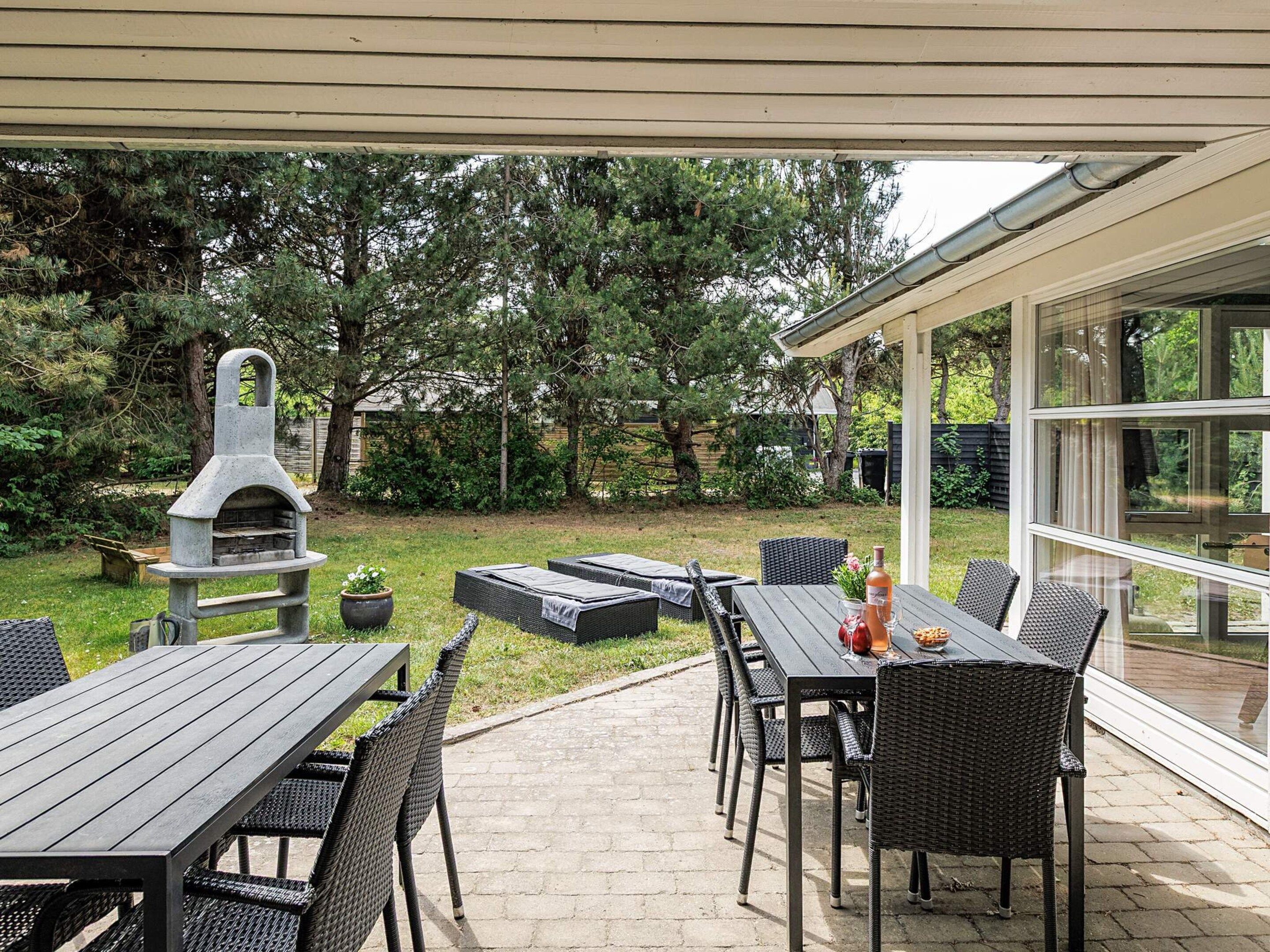 Um pátio externo com churrasqueira de pedra, móveis de vime e área de refeições com paredes de vidro.