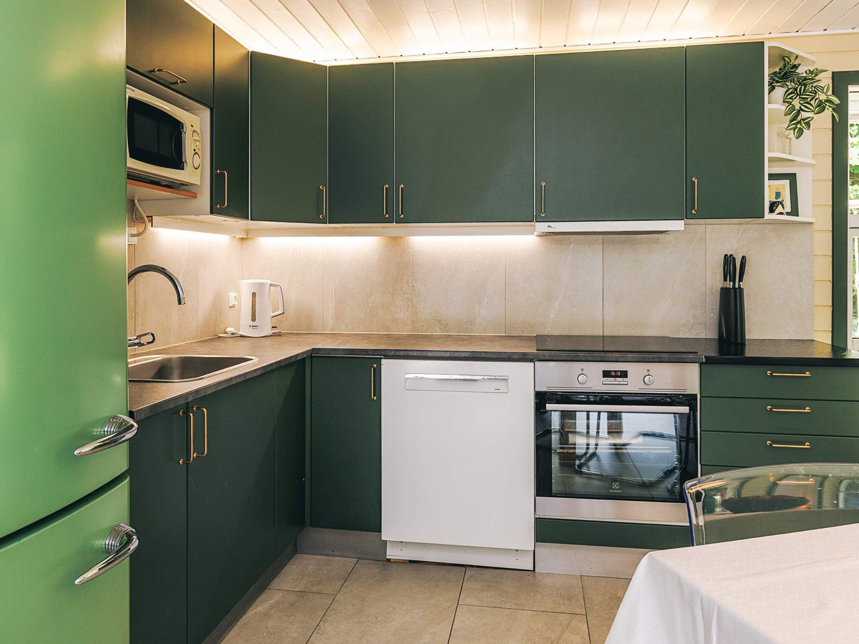 Uma cozinha compacta com armários verdes, uma lava-louças branca, um fogão e um micro-ondas.