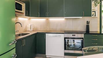 Uma cozinha compacta com armários verdes, uma lava-louças branca, um fogão e um micro-ondas.