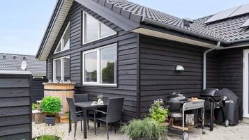 Uma casa moderna com um espaço de pátio que inclui churrasqueira, área de estar externa e vasos de plantas.
